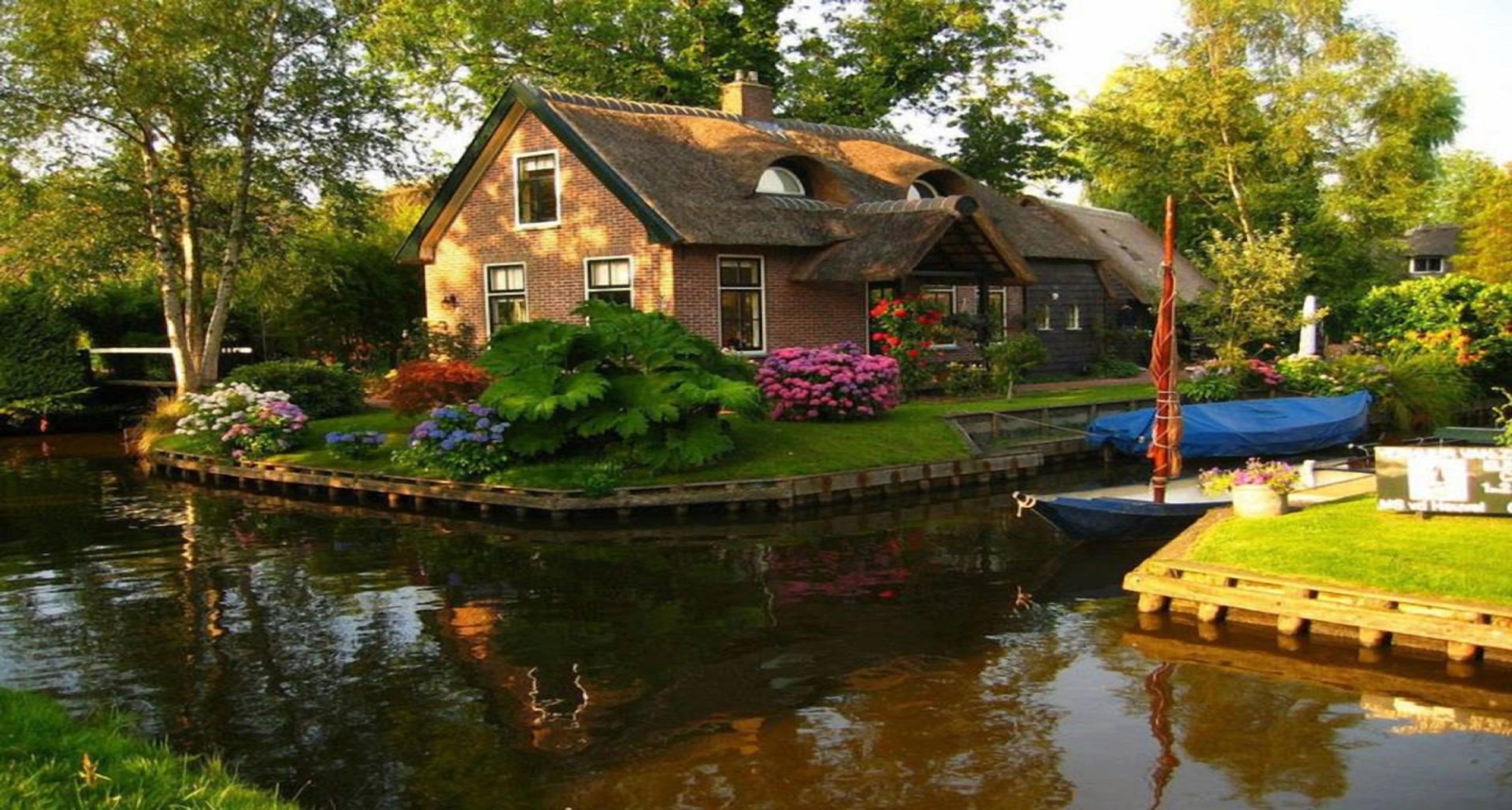 Spring Serenity: Thatched Cottage by Canal with Blooming Flowers and Boat